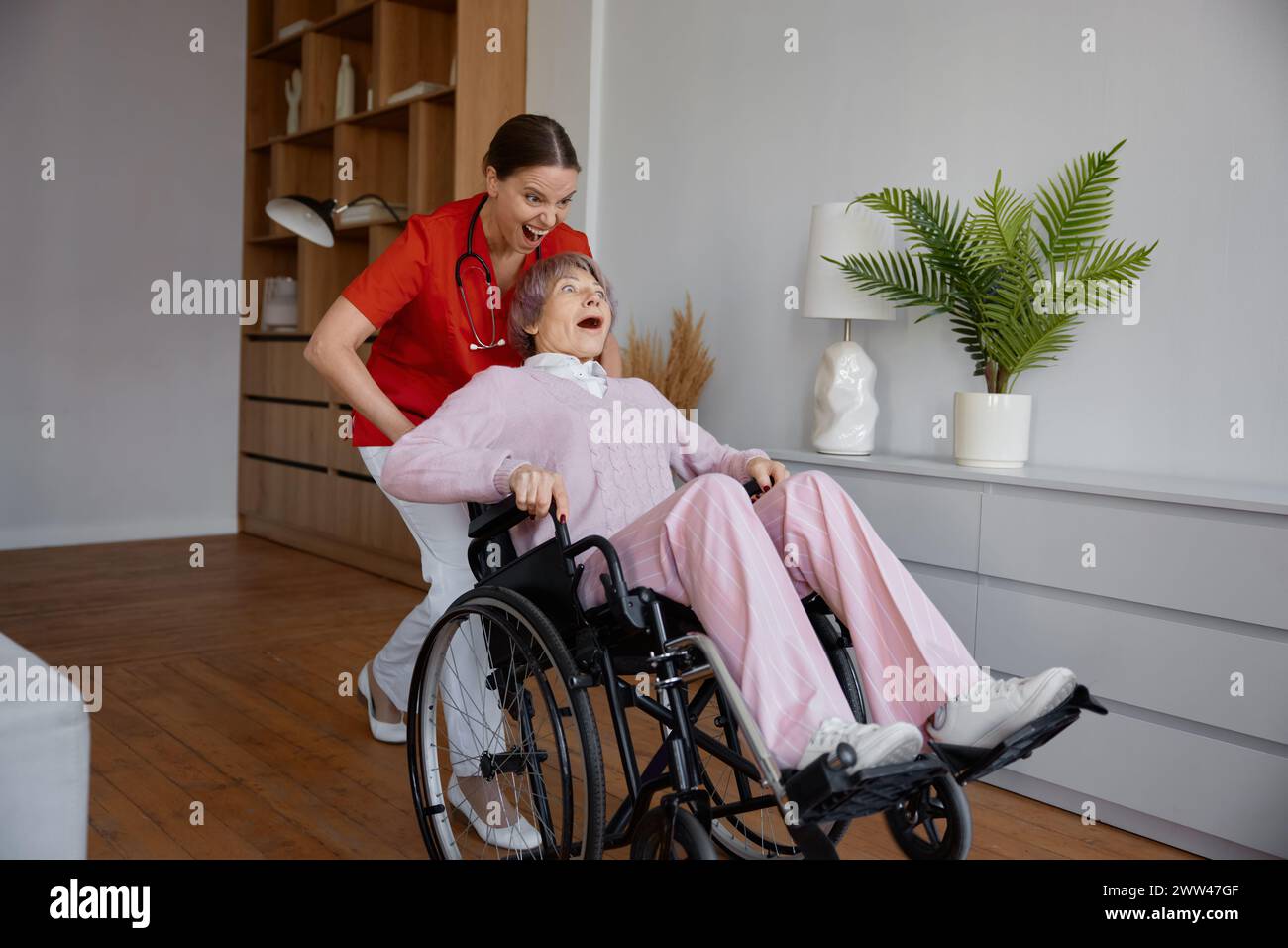 Crazy woman caregiver riding fast elderly woman patient on wheelchair ...