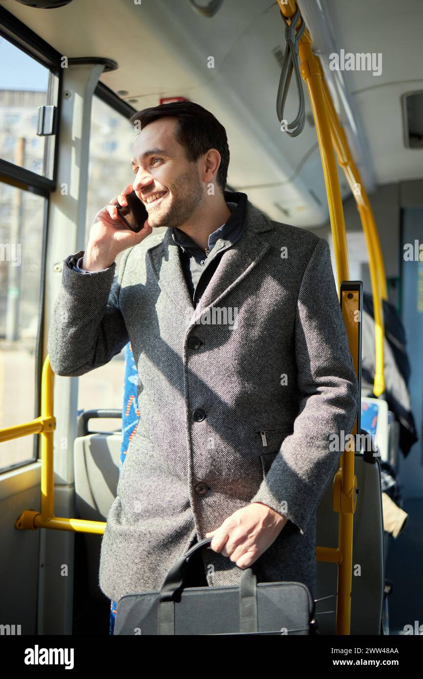 Man in grey coat standing in modern tram, talking on mobile phone wit ...