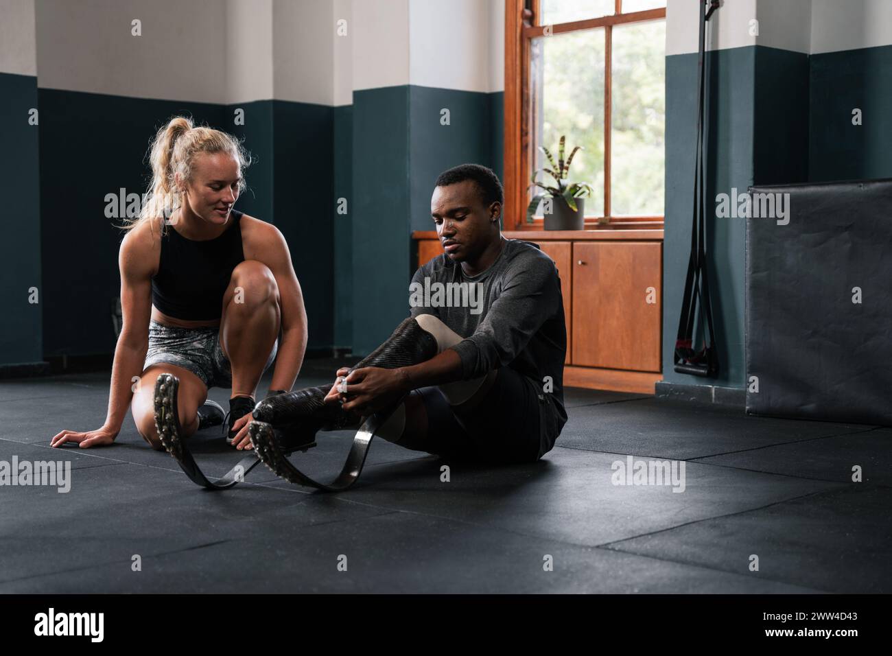 A man and a woman with prosthetic legs are sitting on the gym floor ...