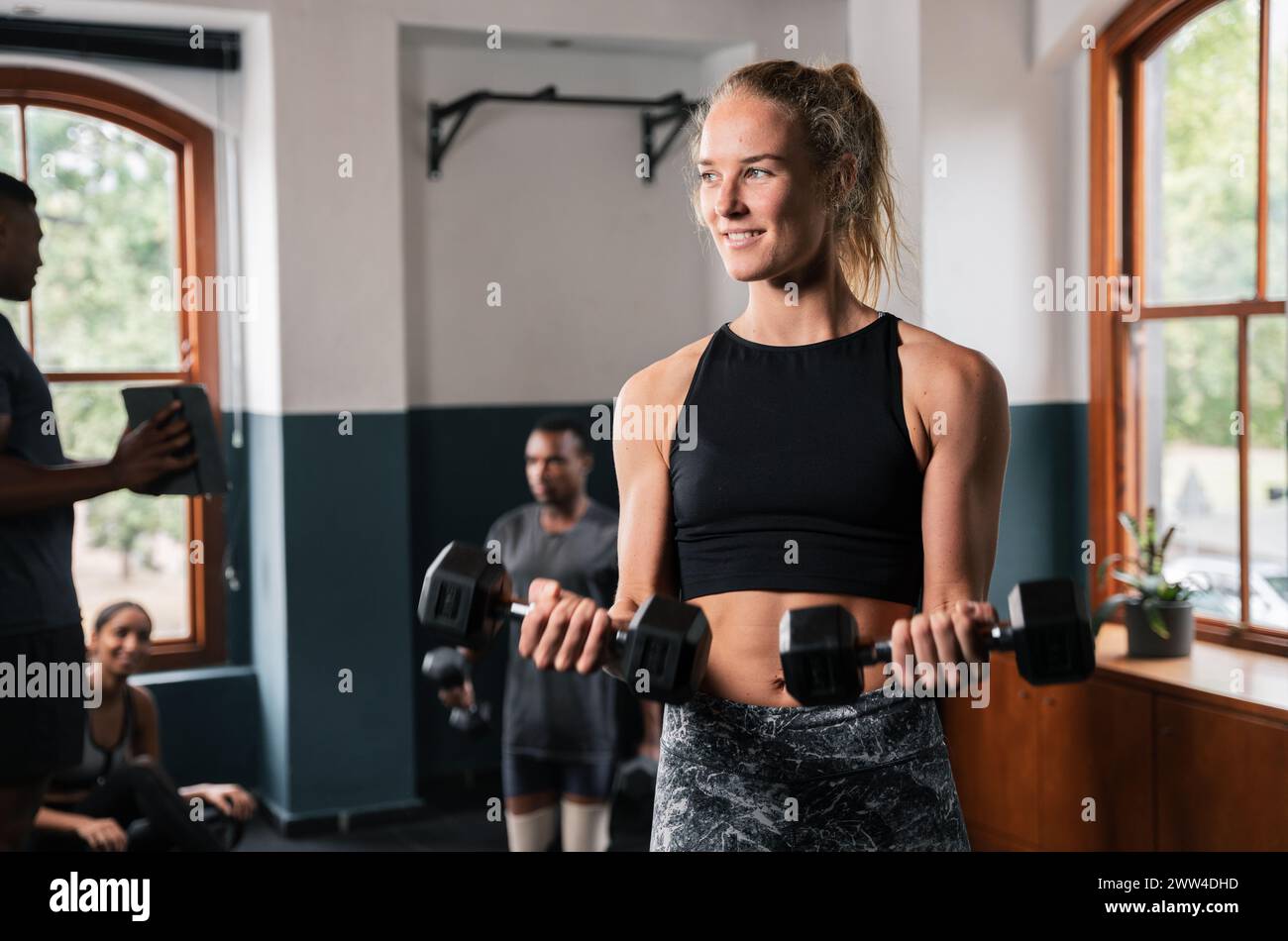 Woman with a big smile lifting dumbbell to strengthen muscle in a gym ...