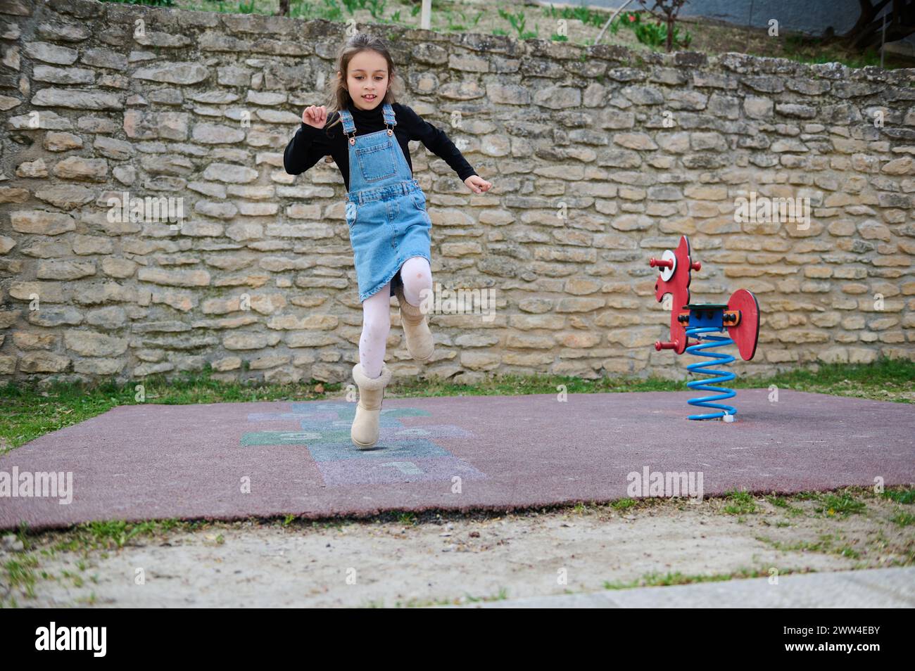 Full length portrait of a little kid girl jumping on one leg, playing ...