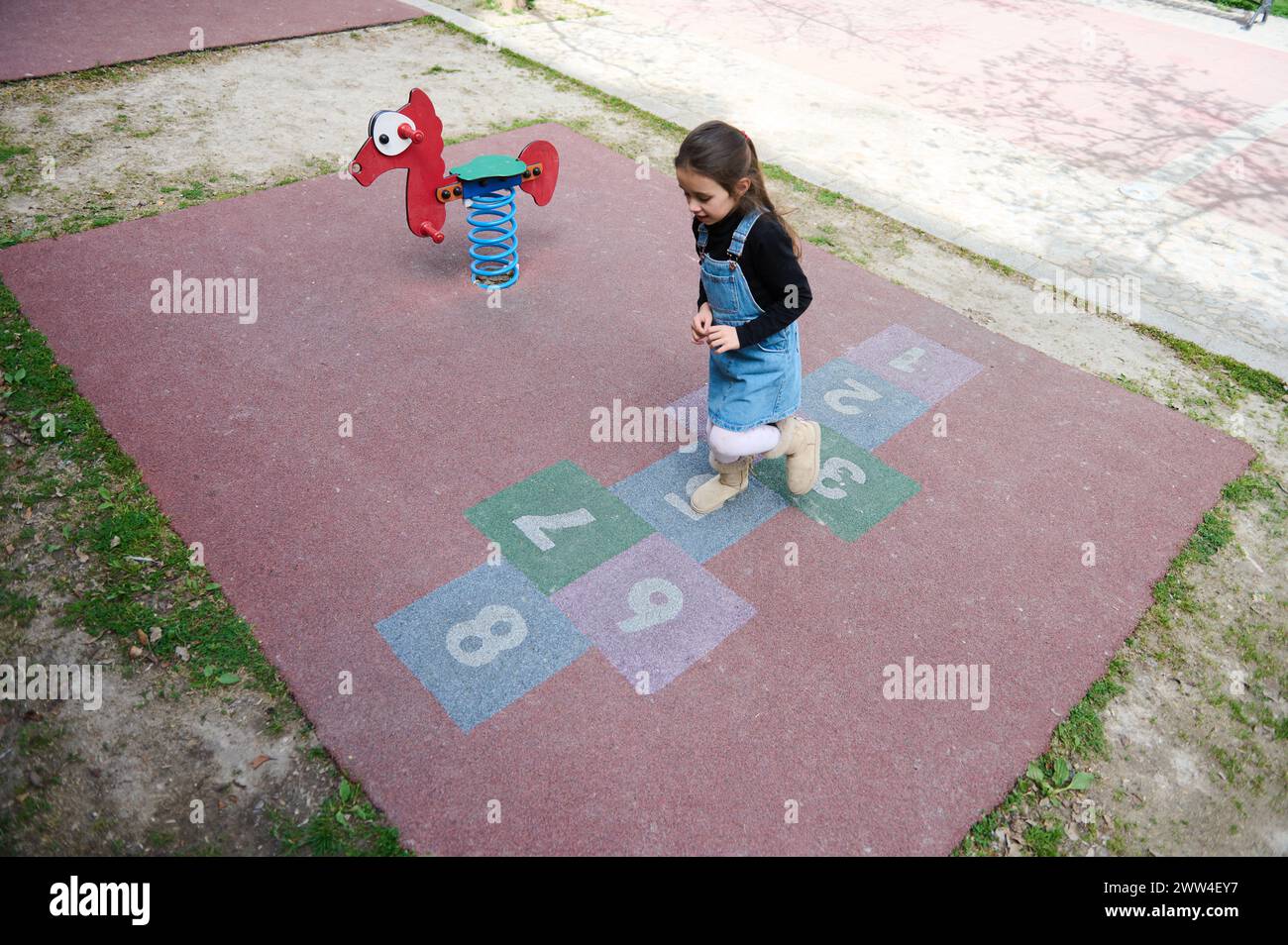 View from above of a kid girl playing hopscotch, taking turns jumping ...