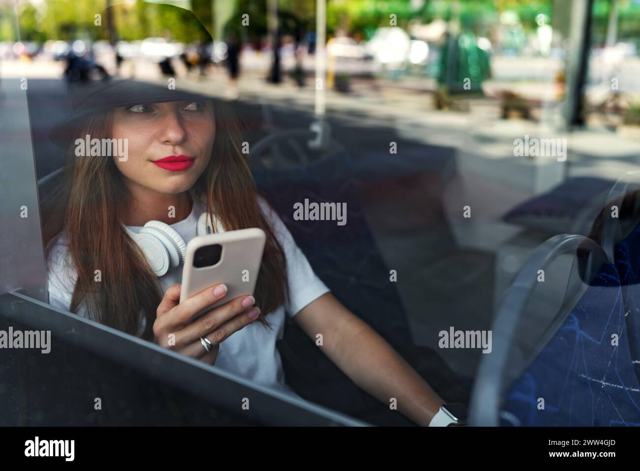 Young pretty urban woman on the bus sits next to the window and uses ...