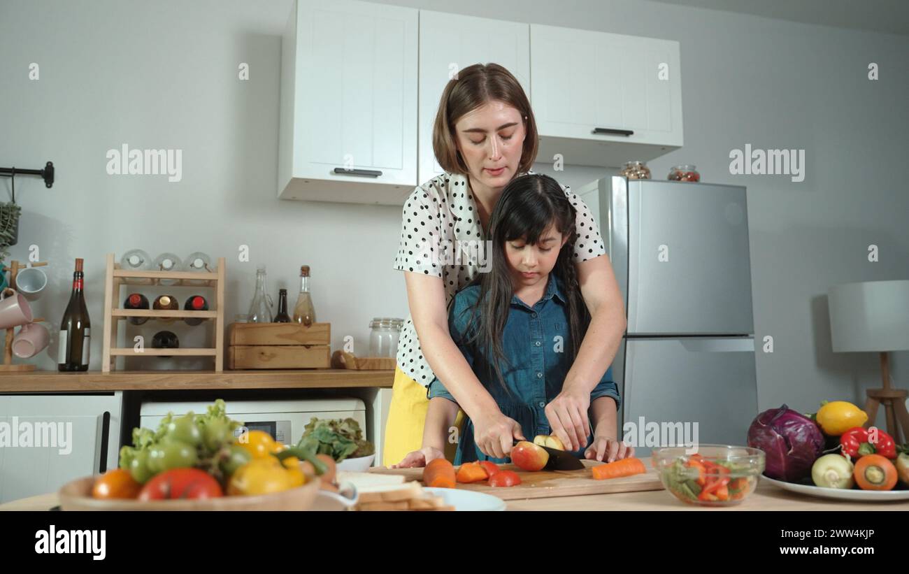 Smart caucasian mother and asian girl cooking together and chopping ...