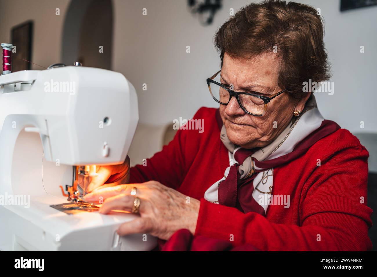 sewing craftswoman in red with glasses sewing a colorful garment Stock ...