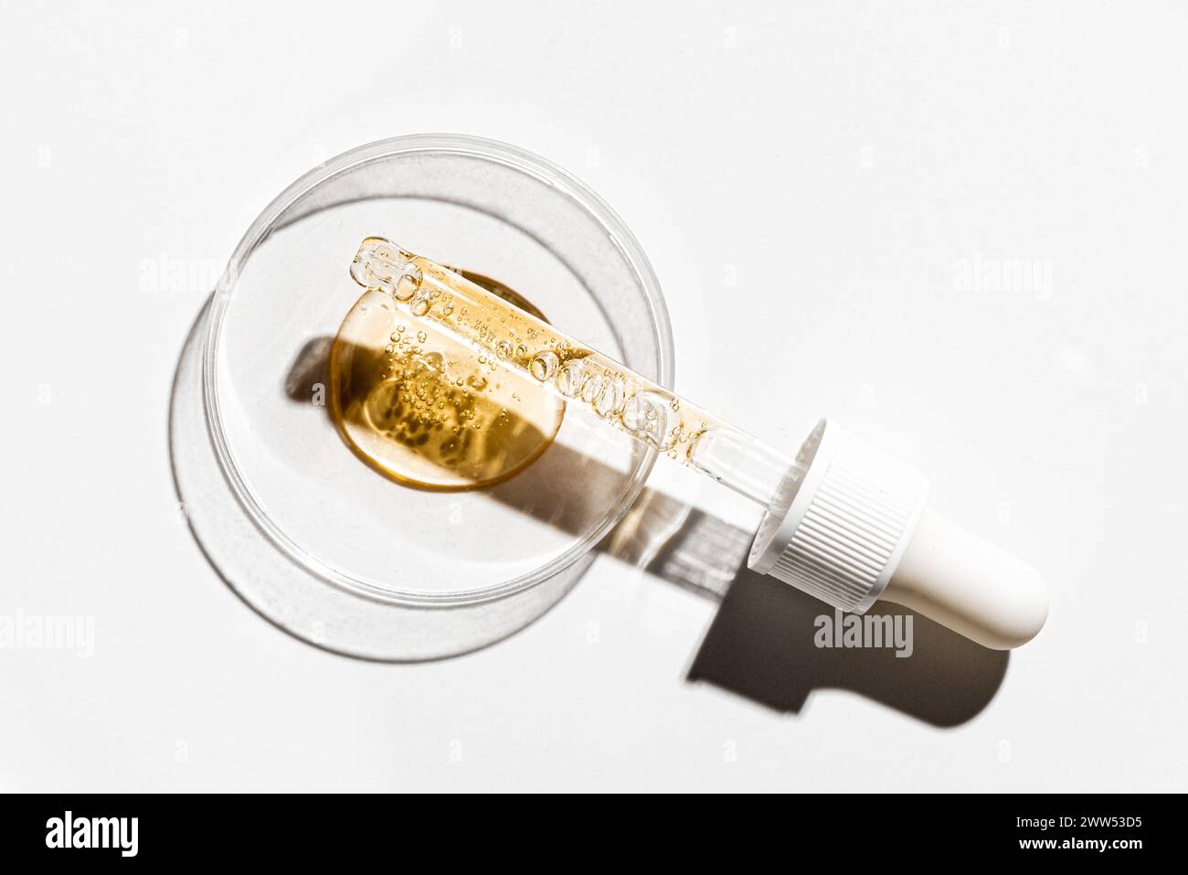 Glass dropper with pouring liquid retinol serum in petri dish. Hard ...