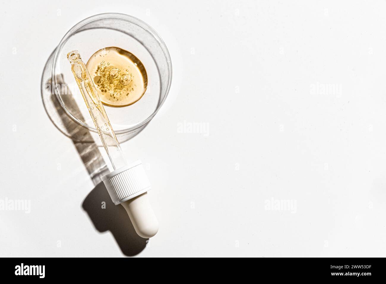 Glass dropper with pouring liquid retinol serum in petri dish. Hard ...