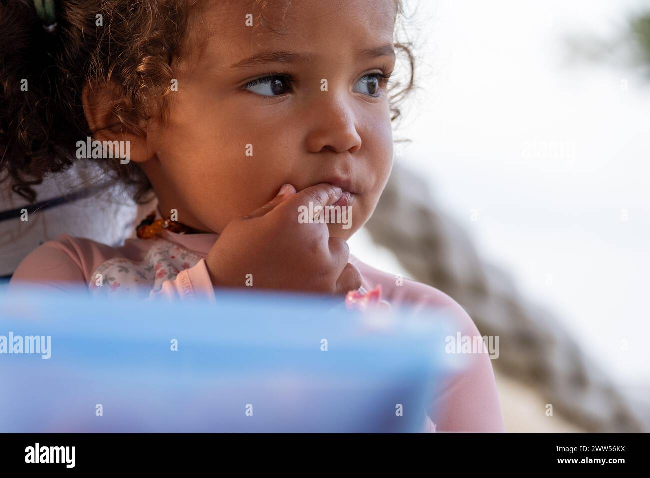 A young child with curly hair and a solemn gaze, thumb gently resting ...
