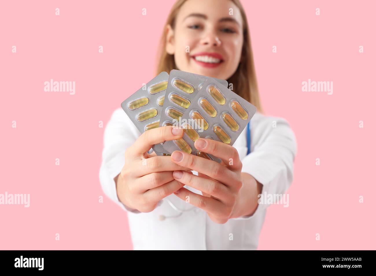 Beautiful doctor with blisters of vitamin supplements on pink ...