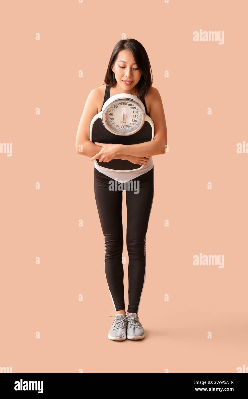 Beautiful young Asian woman with scales on beige background. Weight ...