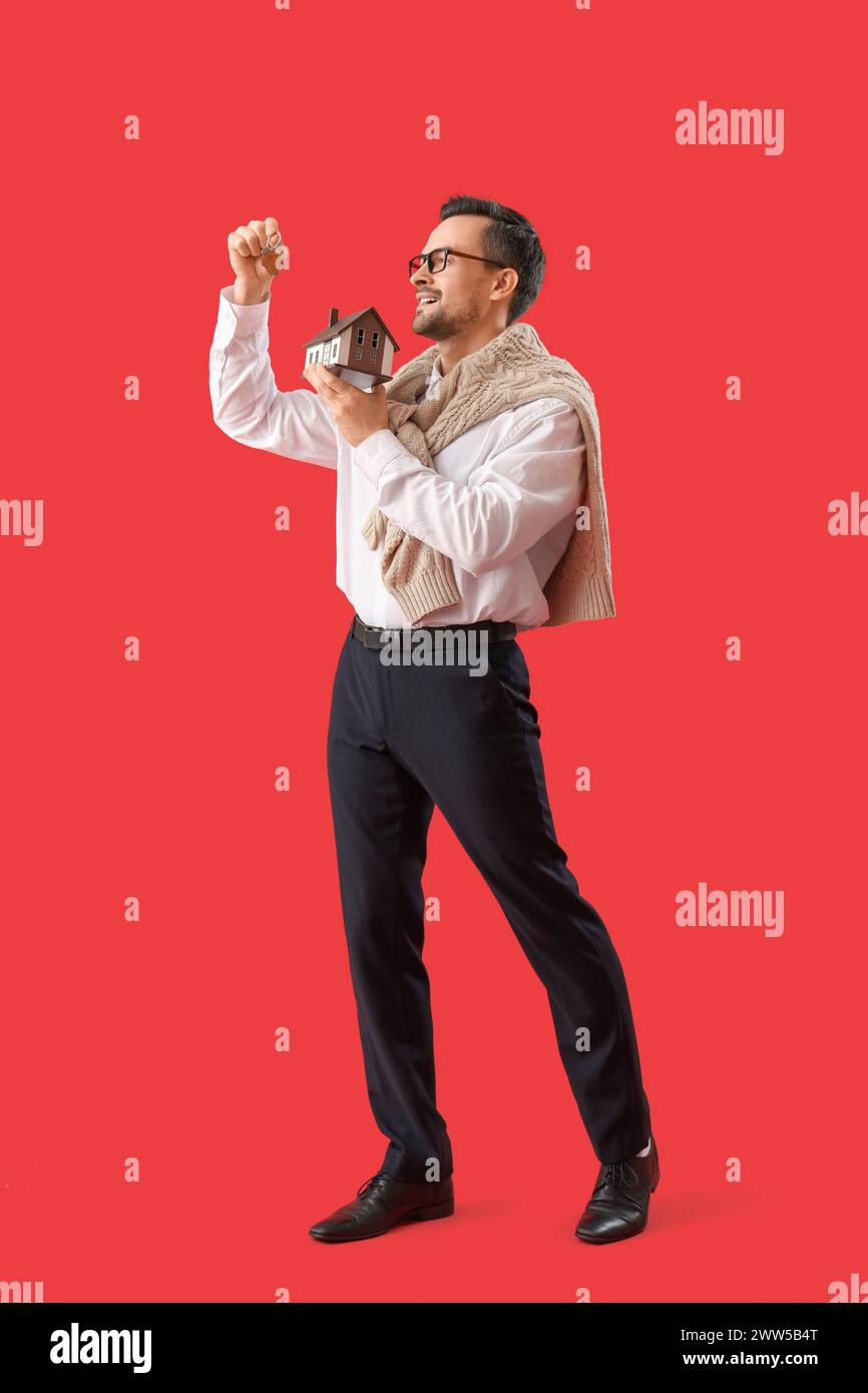Portrait of male real estate agent with house model and keys on red ...