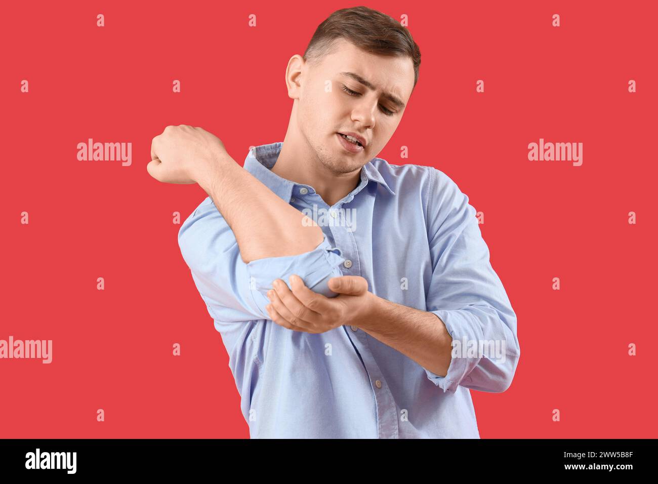 Young man suffering from arm pain on red background Stock Photo - Alamy
