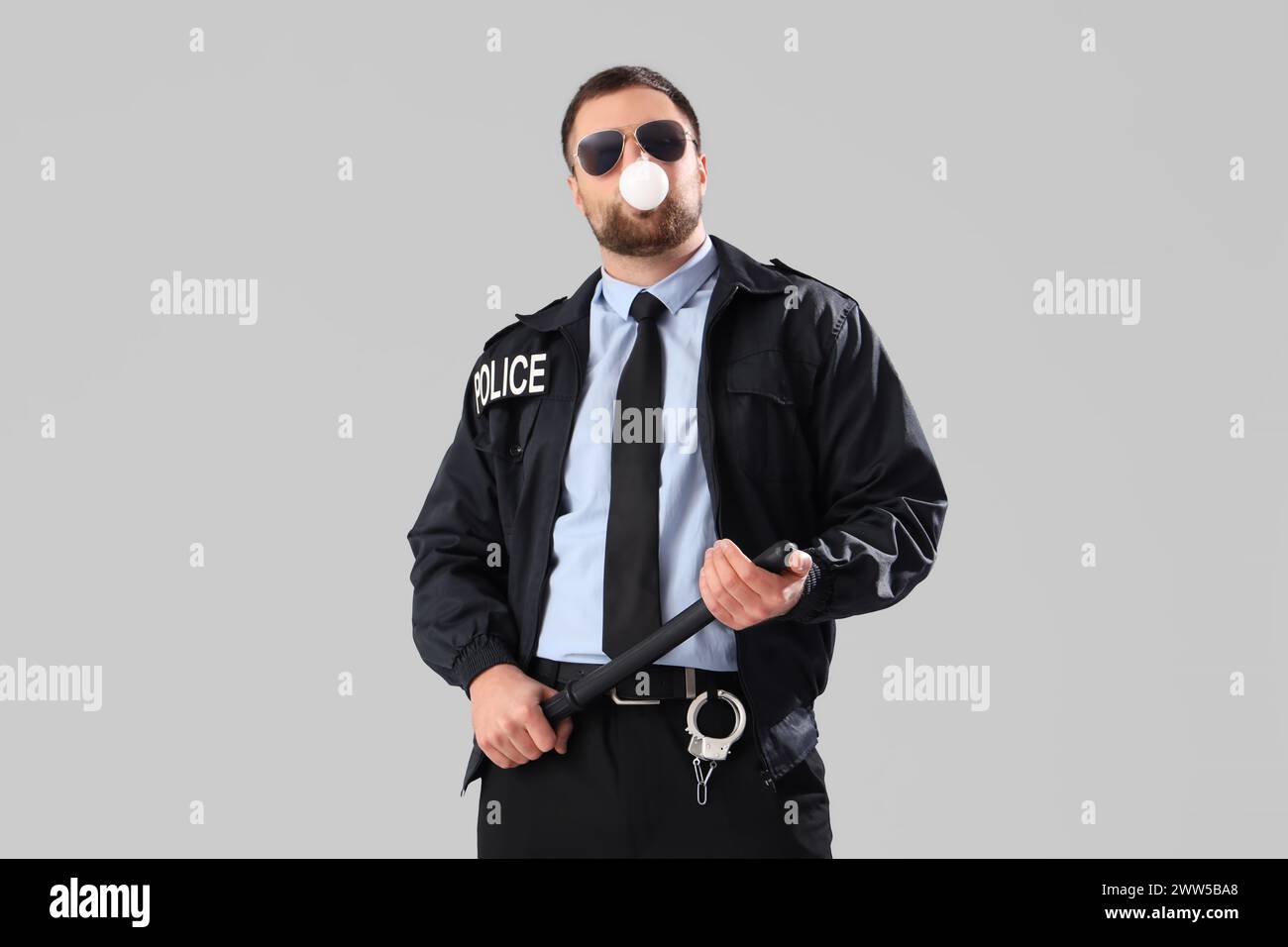 Male police officer with baton blowing bubble gum on grey background ...