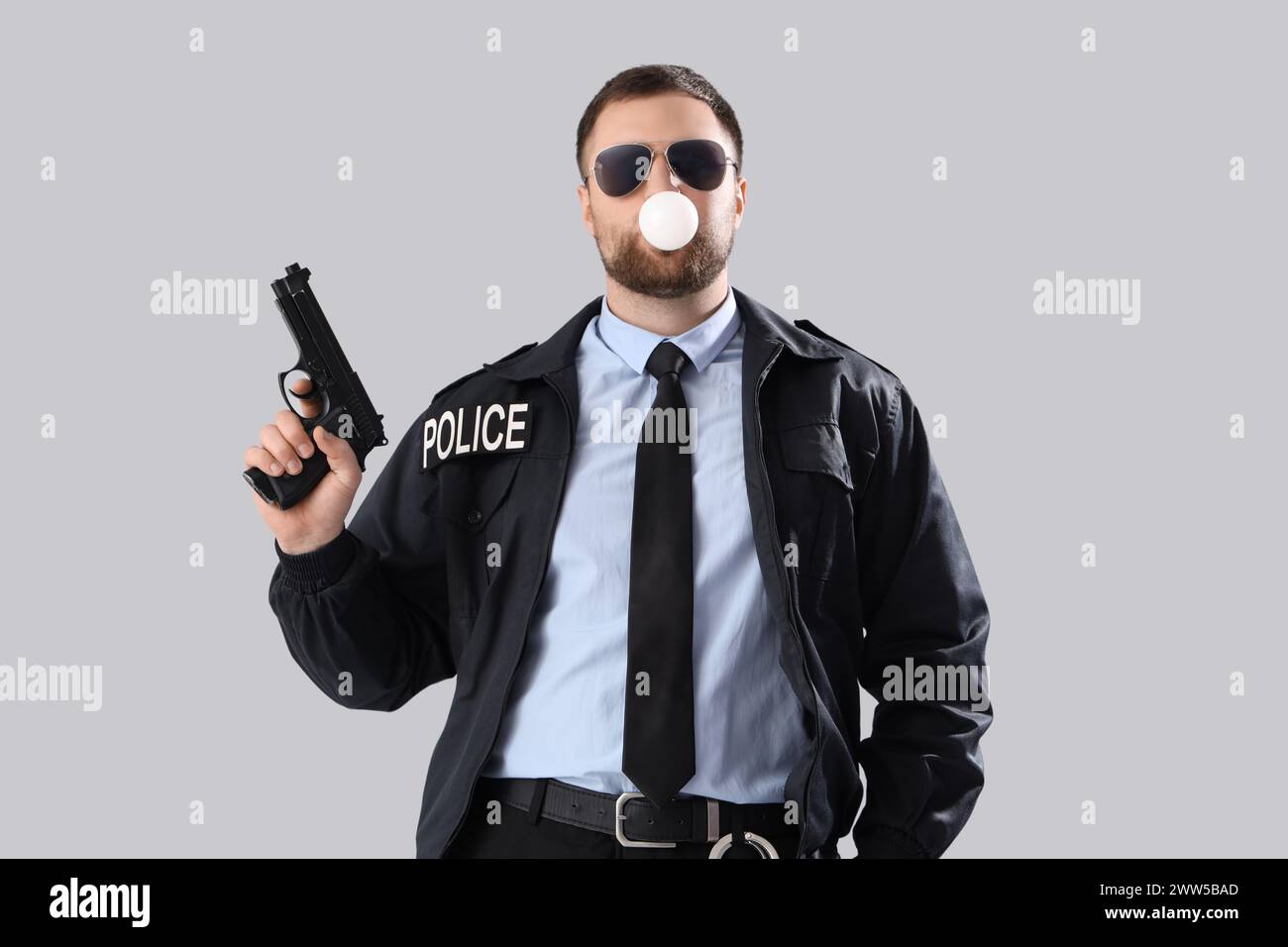 Male police officer with gun blowing bubble gum on grey background ...