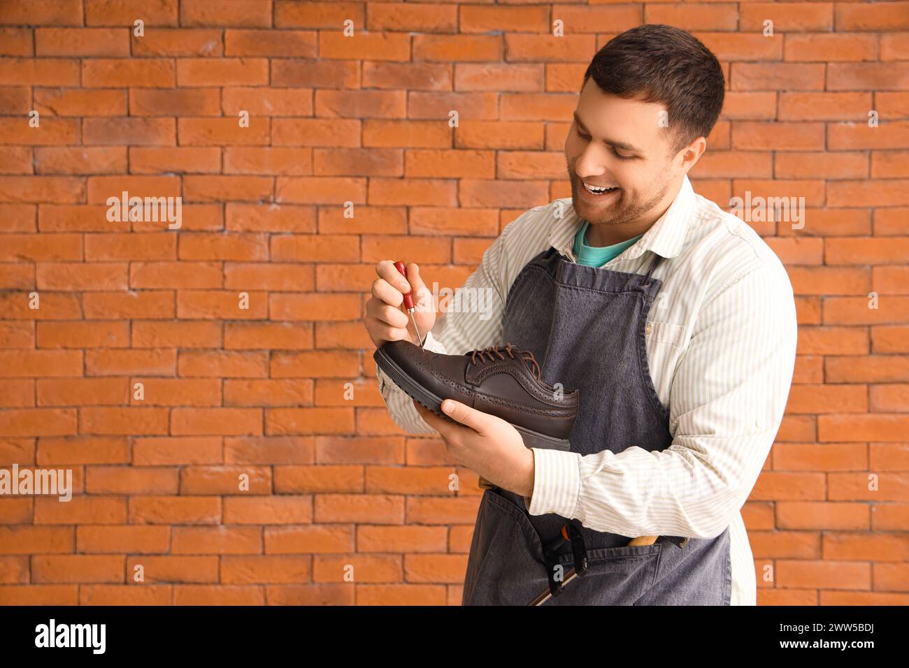 Male shoemaker repairing boot on brick background Stock Photo - Alamy