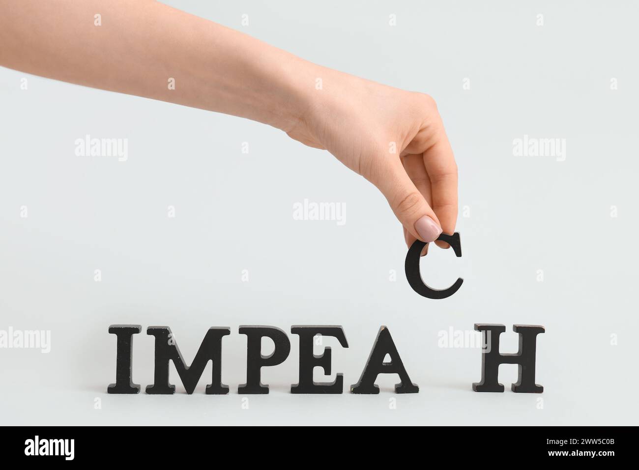 Female hand with wooden letters spelling word IMPEACHMENT on white ...