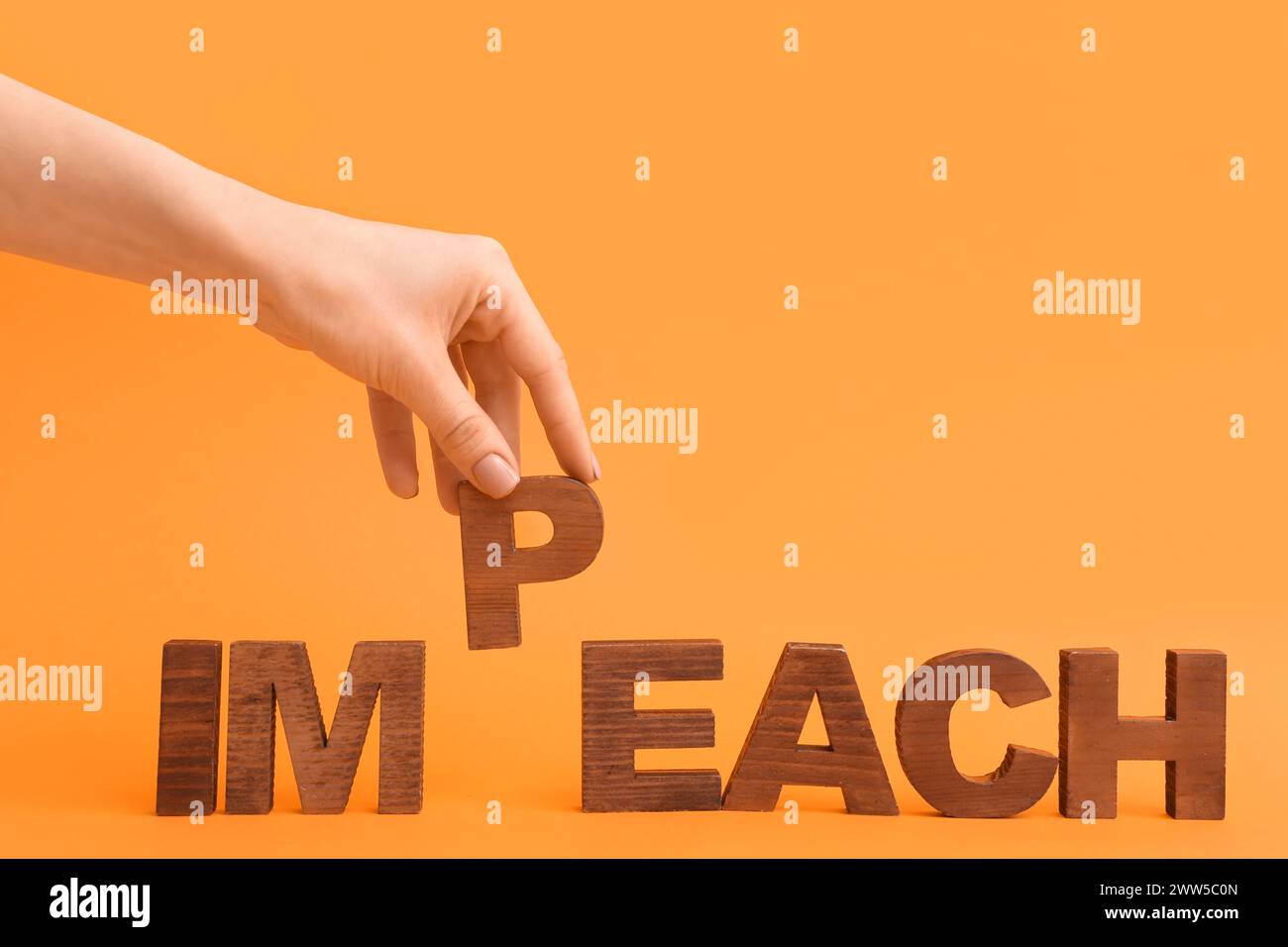 Female hand with wooden letters spelling word IMPEACHMENT on orange ...