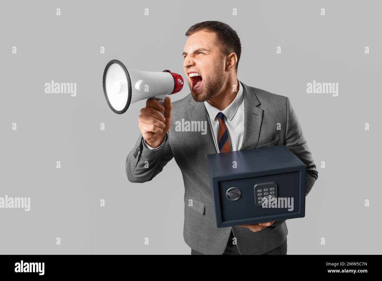 Young man with safe box and megaphone screaming on grey background ...