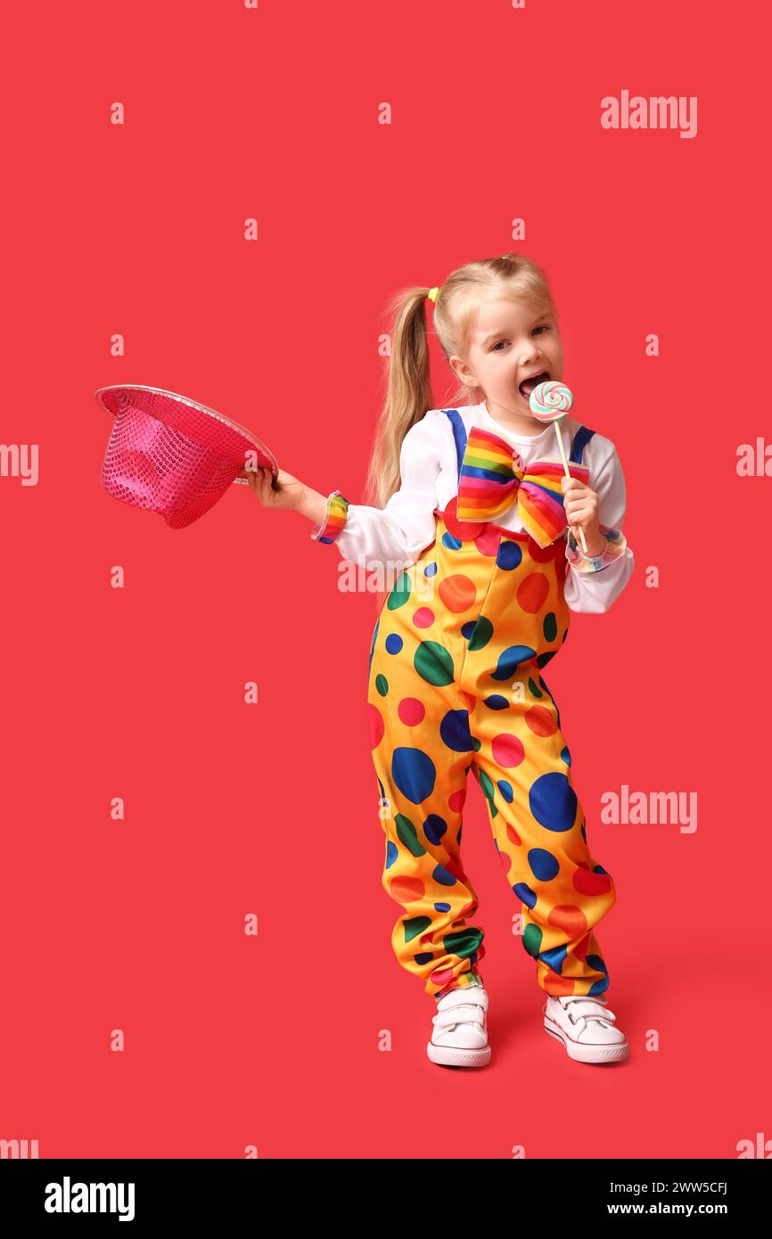 Funny little girl in clown costume with hat and lollipop on red ...