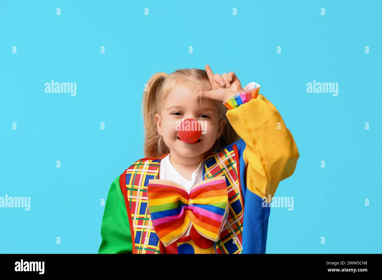 Smiling girl in clown costume showing looser gesture on blue background ...