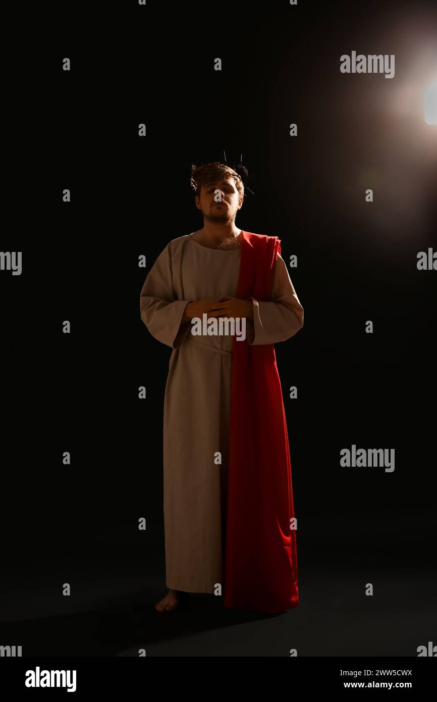 Man in Jesus robe and crown of thorns with light on black background ...