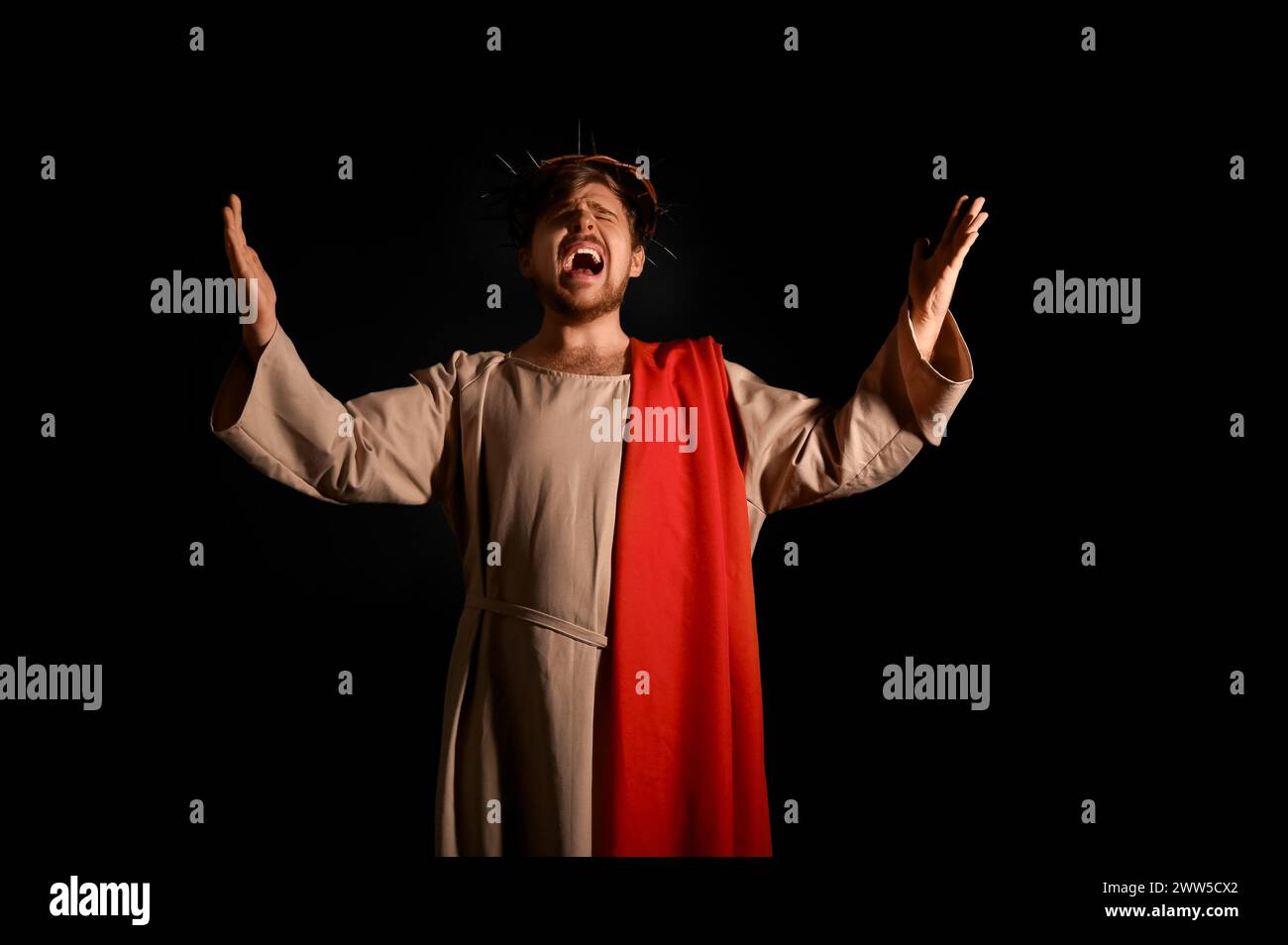 Man in Jesus robe and crown of thorns screaming with light on black ...