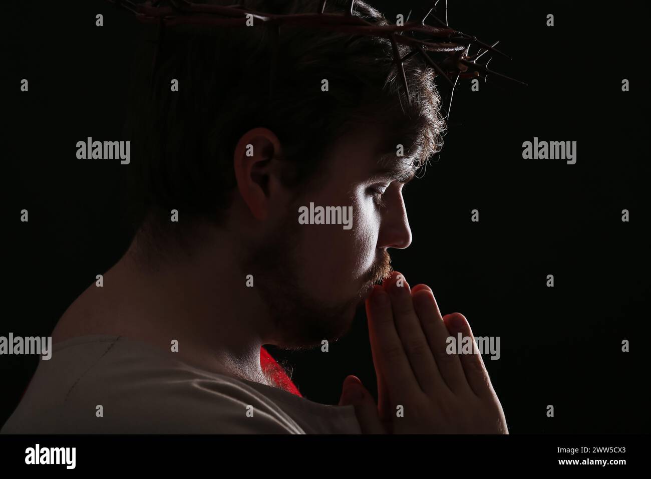 Man in Jesus robe and crown of thorns praying with light on black ...