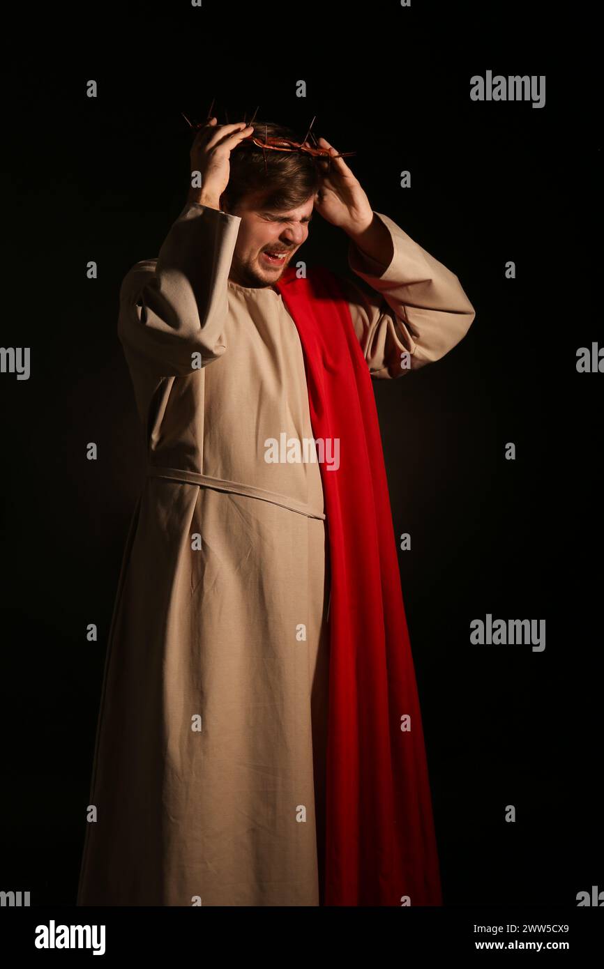 Man in Jesus robe and crown of thorns screaming with light on black ...
