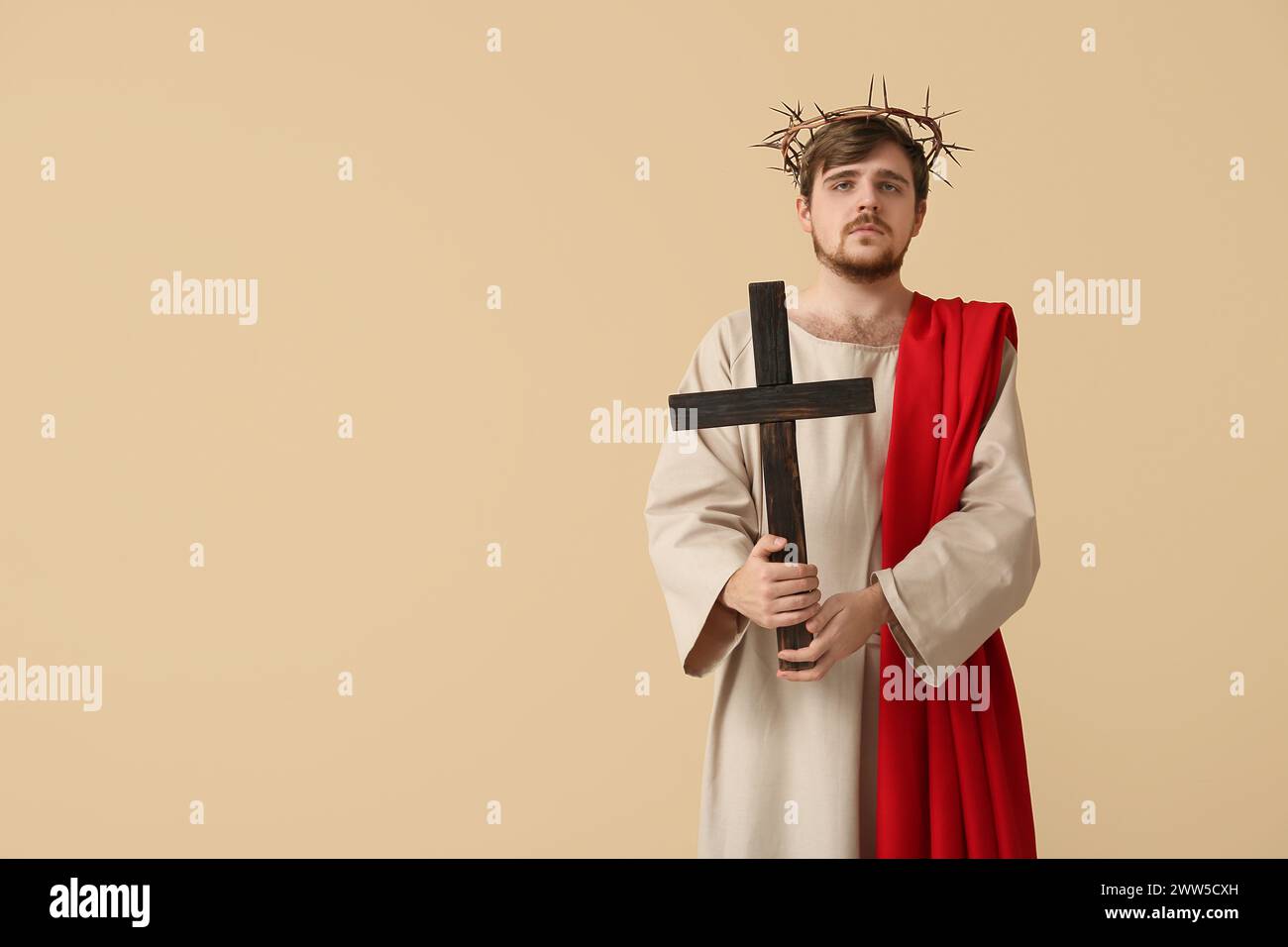 Man in Jesus robe and crown of thorns with wooden cross on beige ...