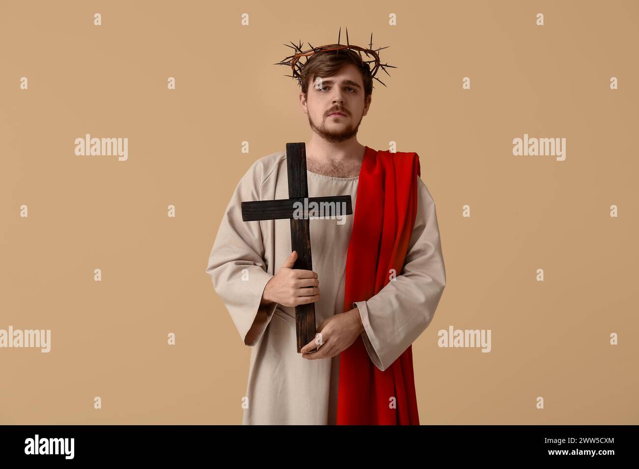 Man in Jesus robe and crown of thorns with wooden cross on beige ...