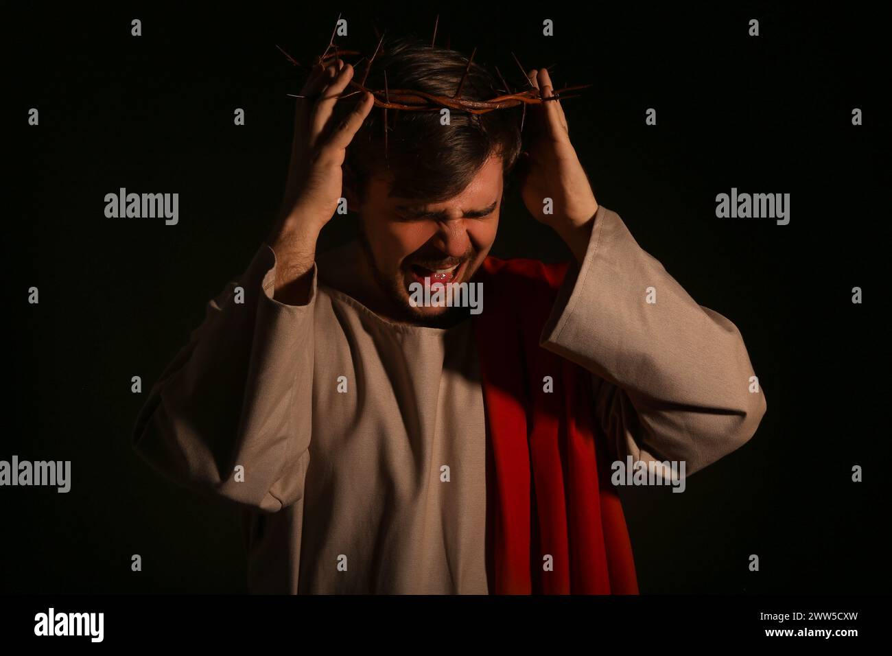 Man in Jesus robe and crown of thorns screaming with light on black ...