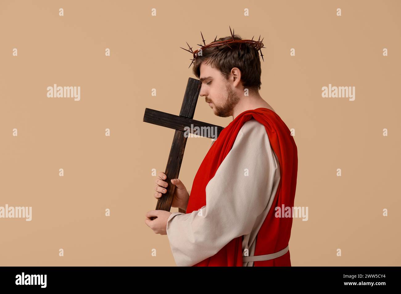 Man in Jesus robe and crown of thorns with wooden cross on beige ...