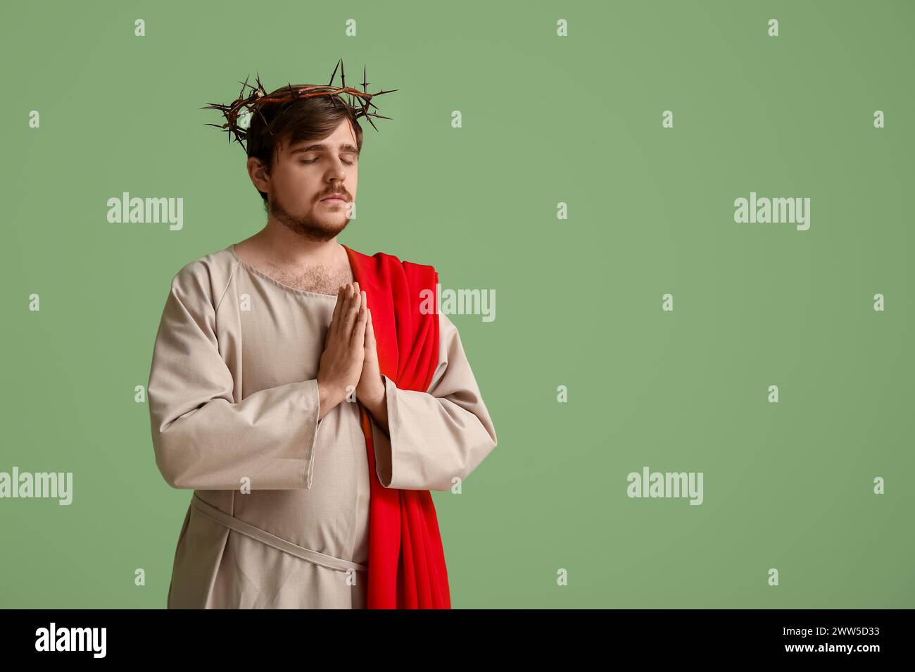 Man in Jesus robe and crown of thorns with blood praying on green ...