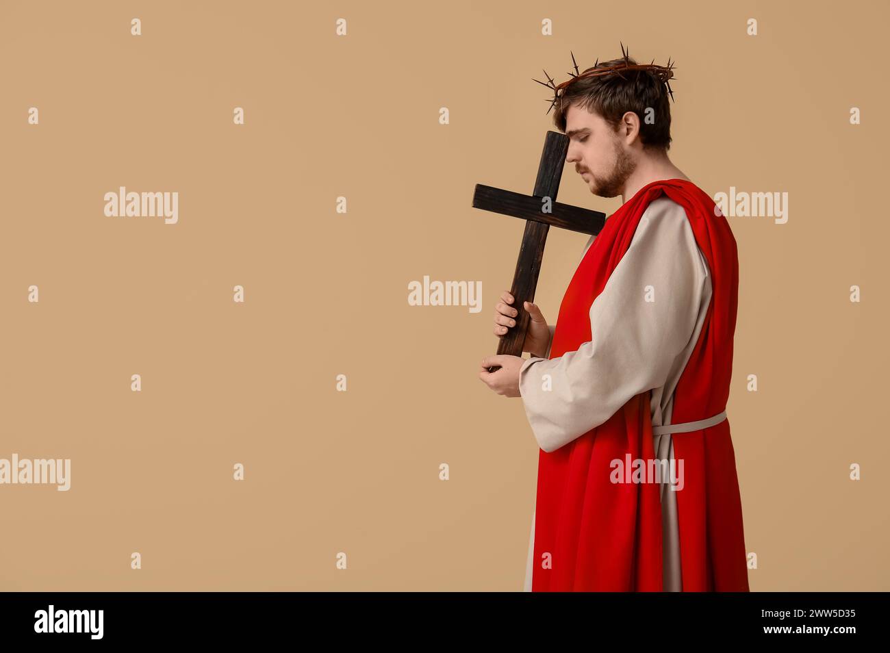 Man in Jesus robe and crown of thorns with wooden cross on beige ...