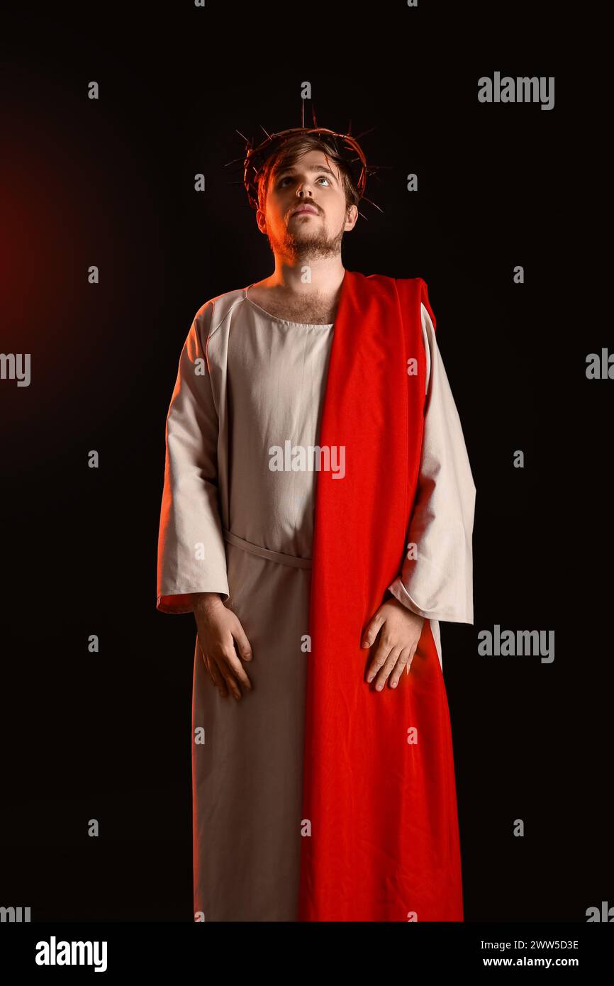 Man in Jesus robe and crown of thorns with red light on black ...