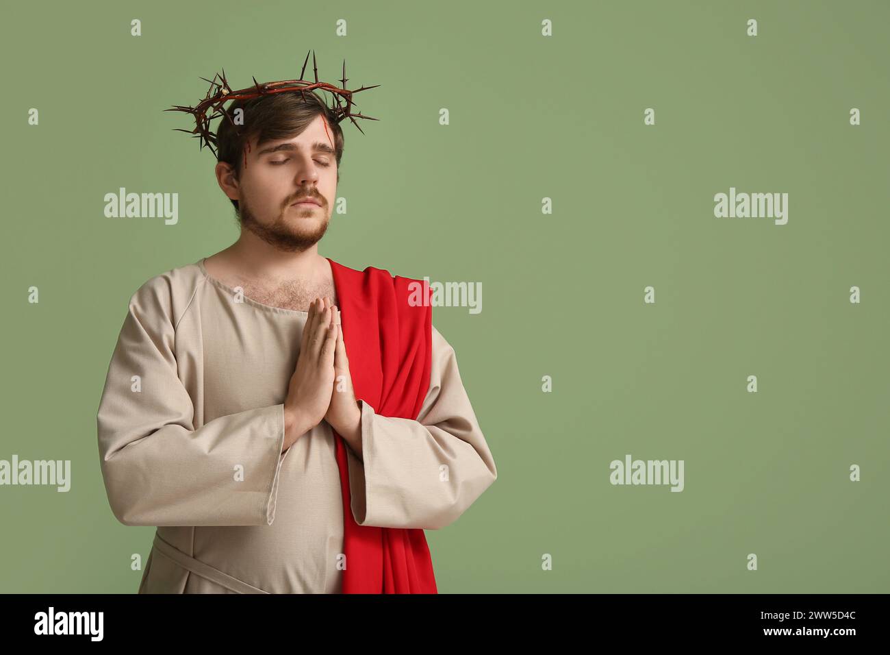 Man in Jesus robe and crown of thorns with blood praying on green ...