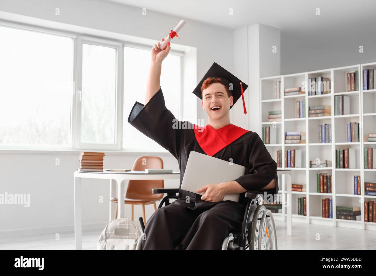Happy male graduate in wheelchair with laptop and diploma at university ...