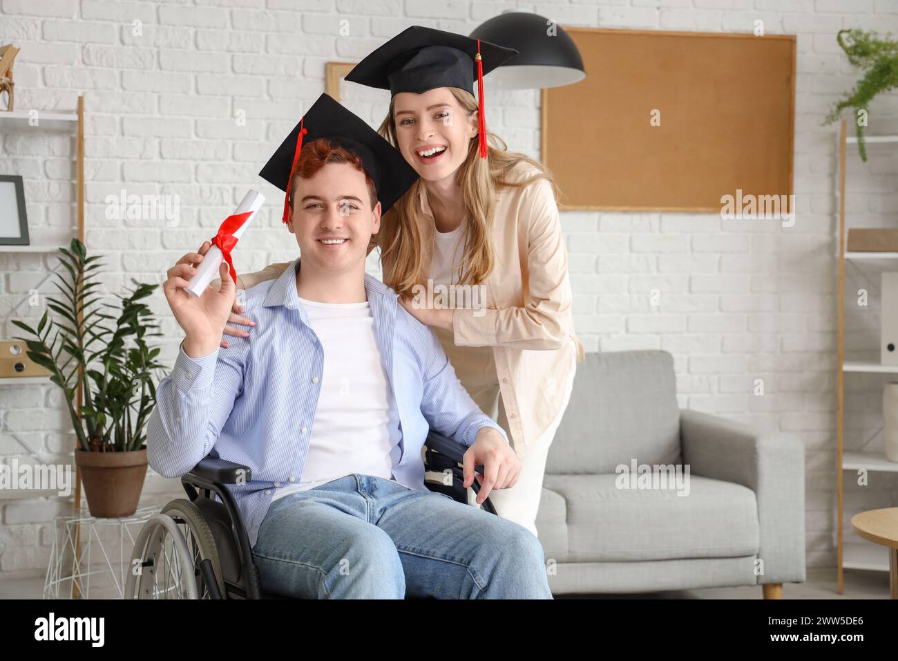 Male graduate in wheelchair with diploma and his classmate at home ...
