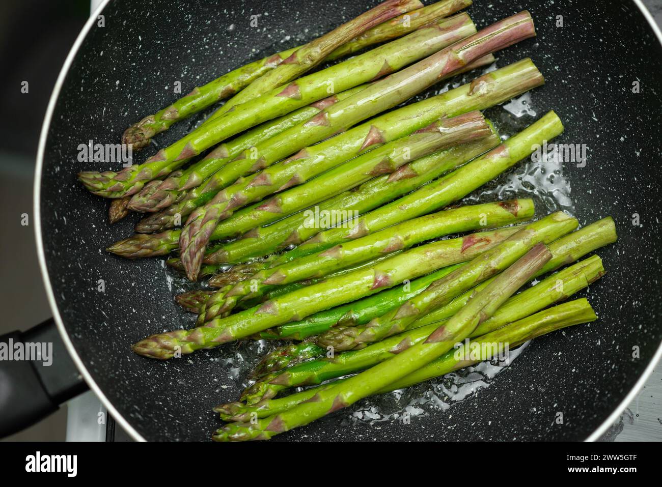 A pan of green asparagus is cooking in a pan. The asparagus are in ...