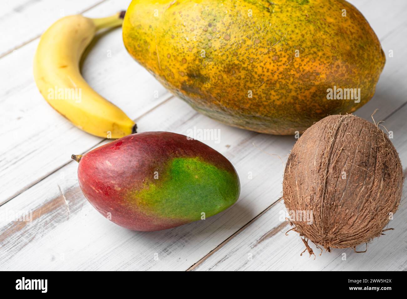 A bunch of bananas, a mango, and a coconut are displayed on a white ...
