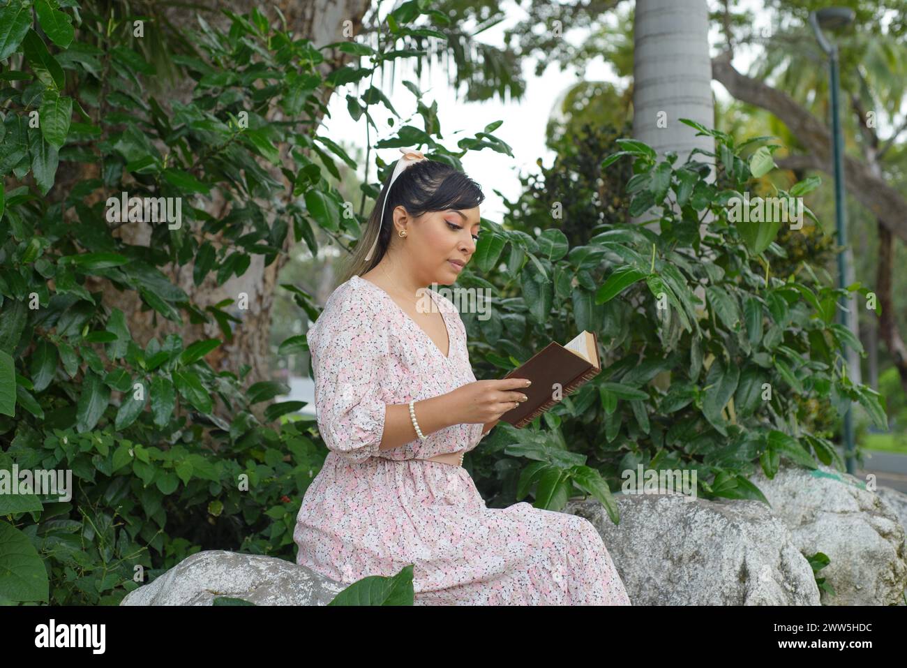 Woman seated next to a tree trunk in a park reading a book. World book ...