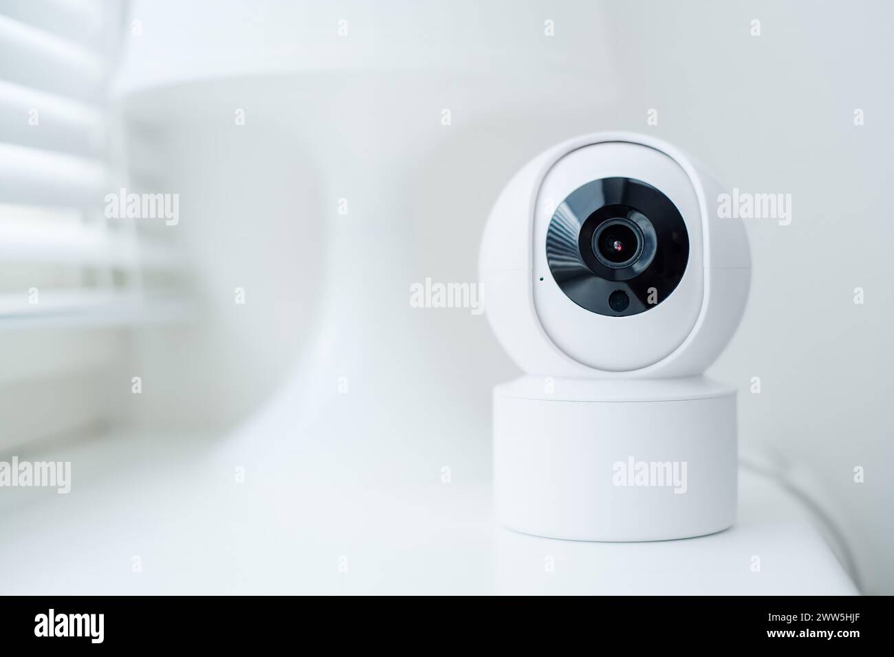 Modern white security camera on a table by a window. Suitable for ...