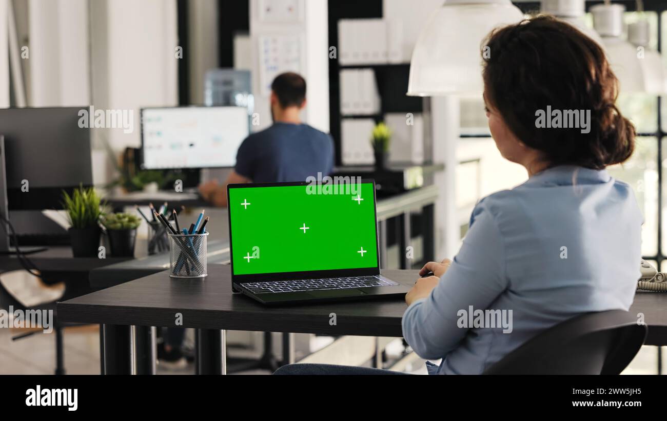 Employee checks greenscreen on laptop, looking at isolated copyspace ...