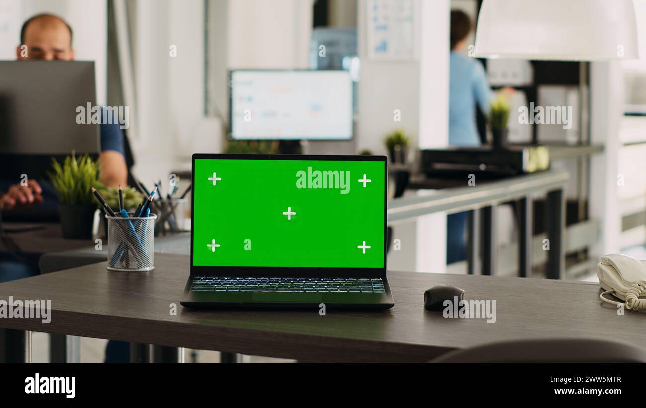Greenscreen laptop in coworking space placed on empty office desk, open floor plan business ...