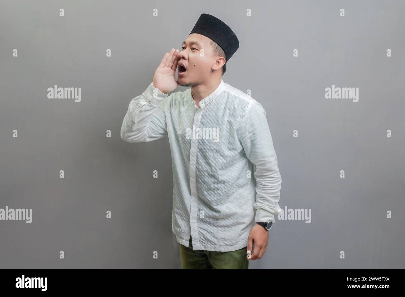 Asian Muslim man shouting and cupping hands around mouth wearing a koko ...