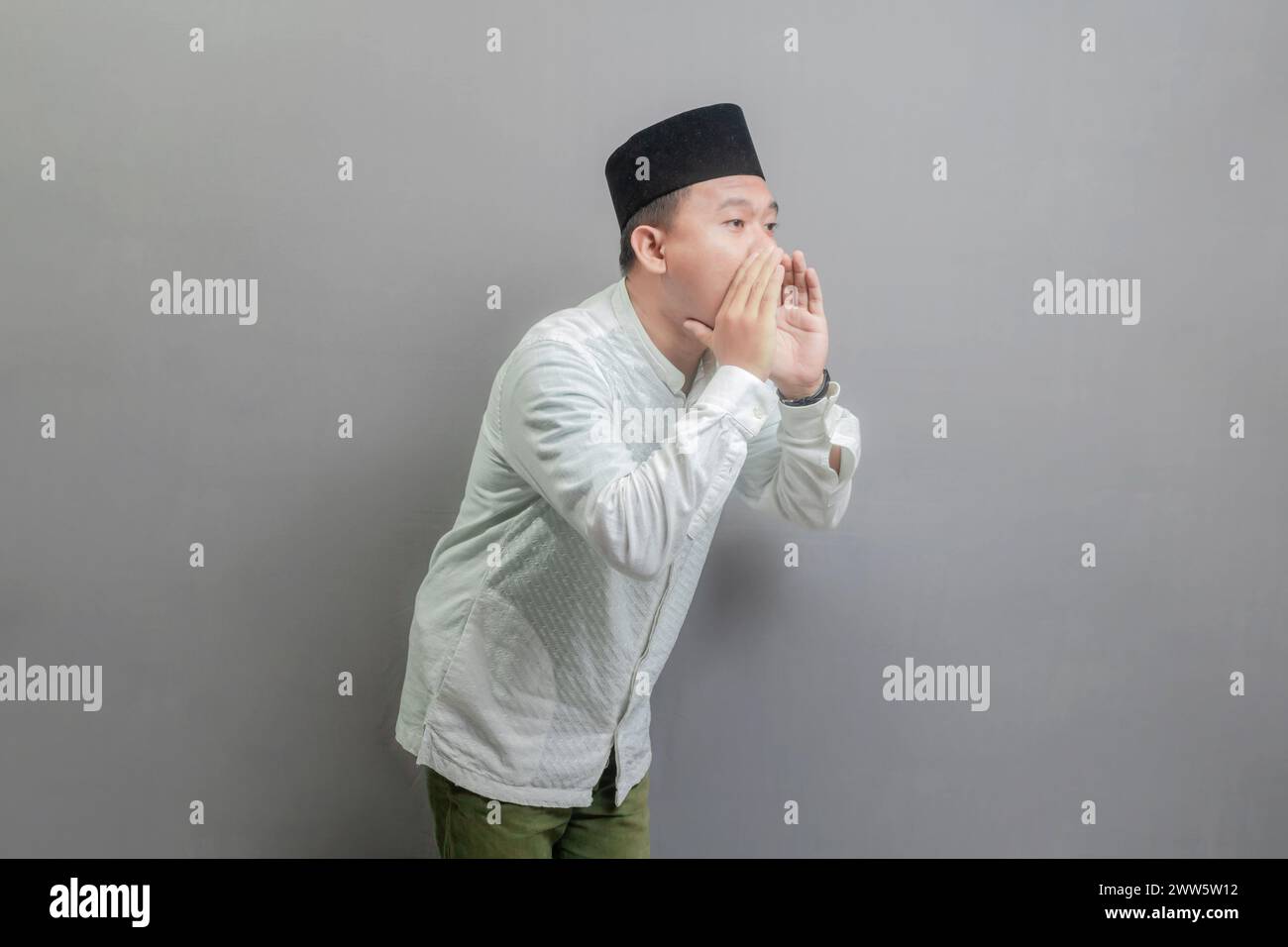 Asian Muslim man shouting and cupping hands around mouth wearing a koko ...