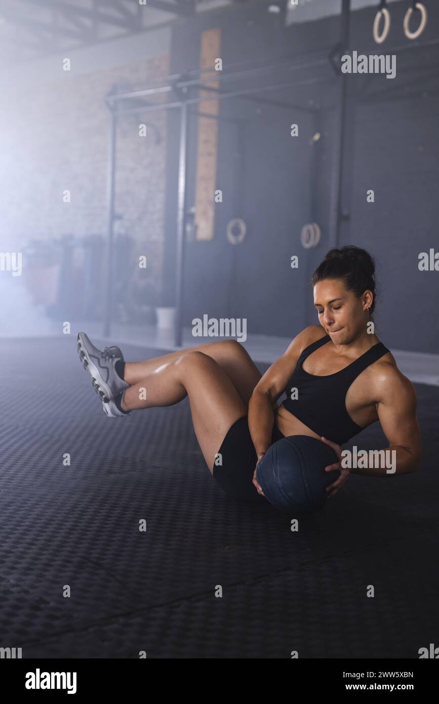 A fit Hispanic woman engages in an ab workout with a medicine ball in a ...