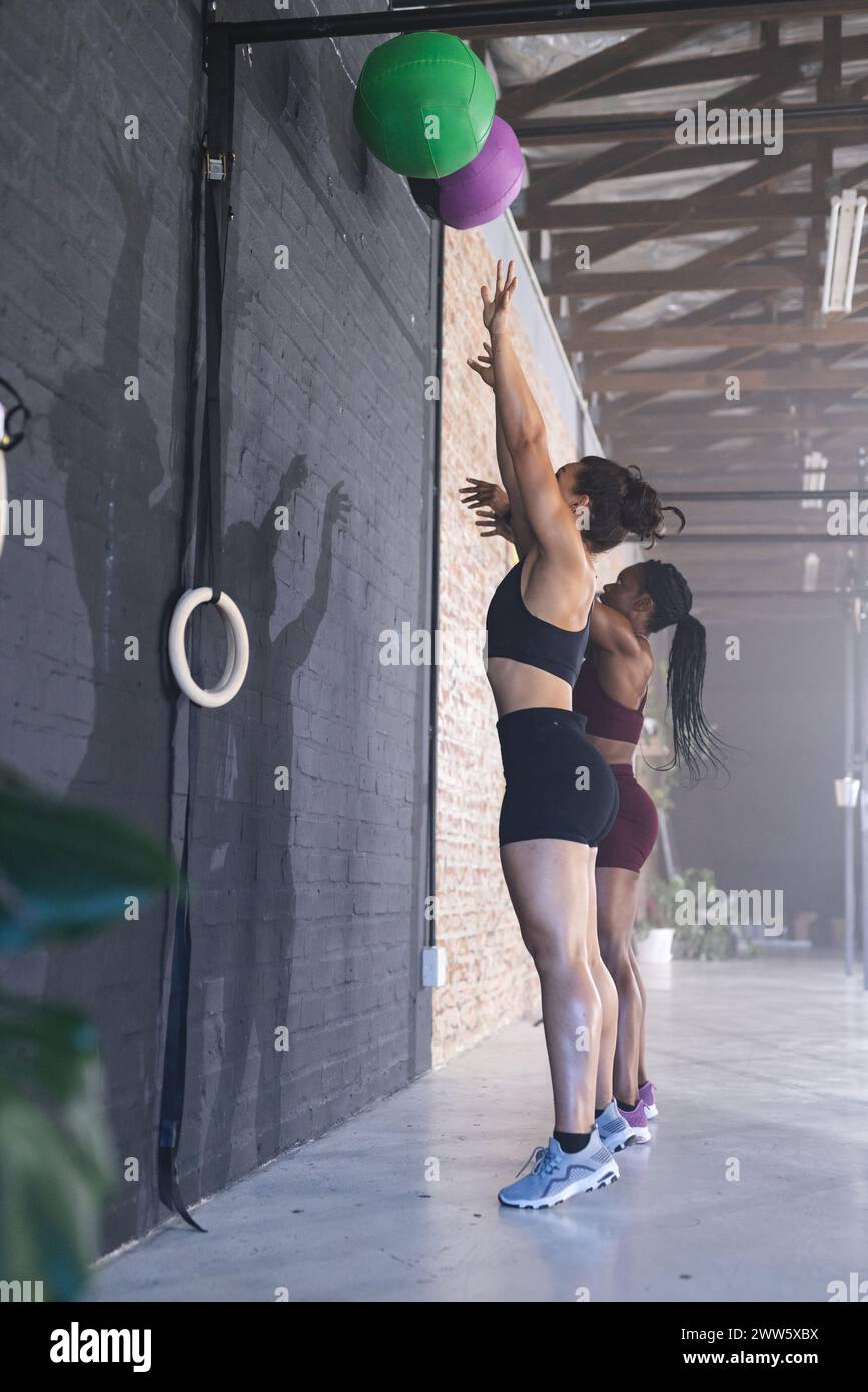 A diverse strong fit women engage in a wall ball exercise in the gym ...