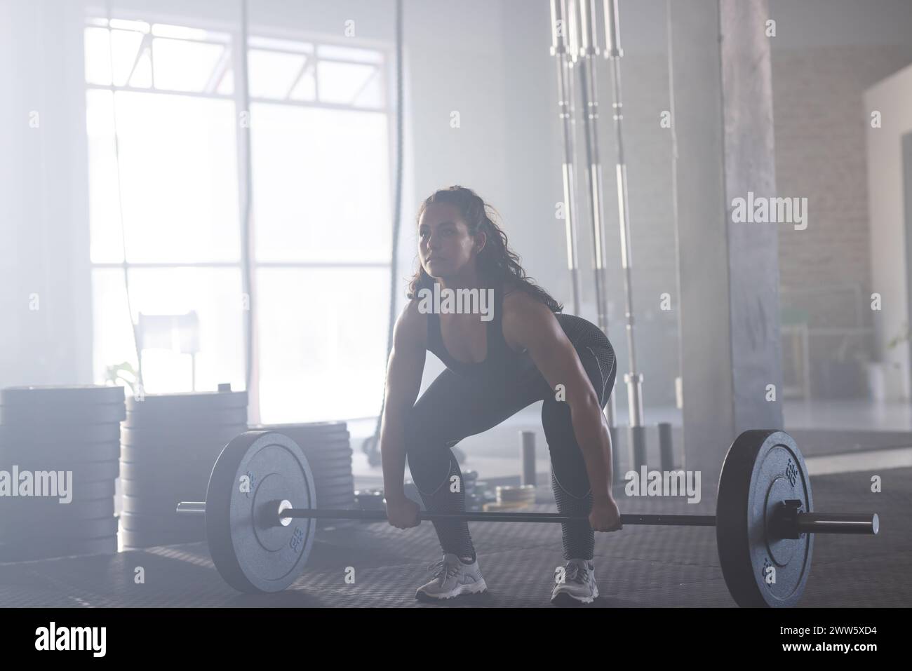 A fit Caucasian woman is performing a deadlift with a barbell in a gym ...