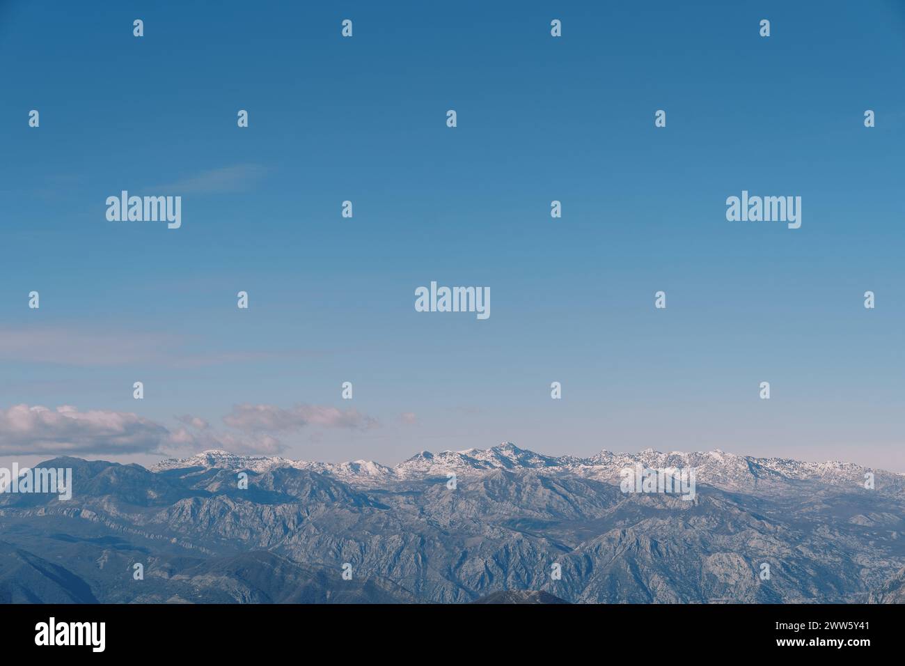 Snow-covered mountain range above the Bay of Kotor against the blue sky ...